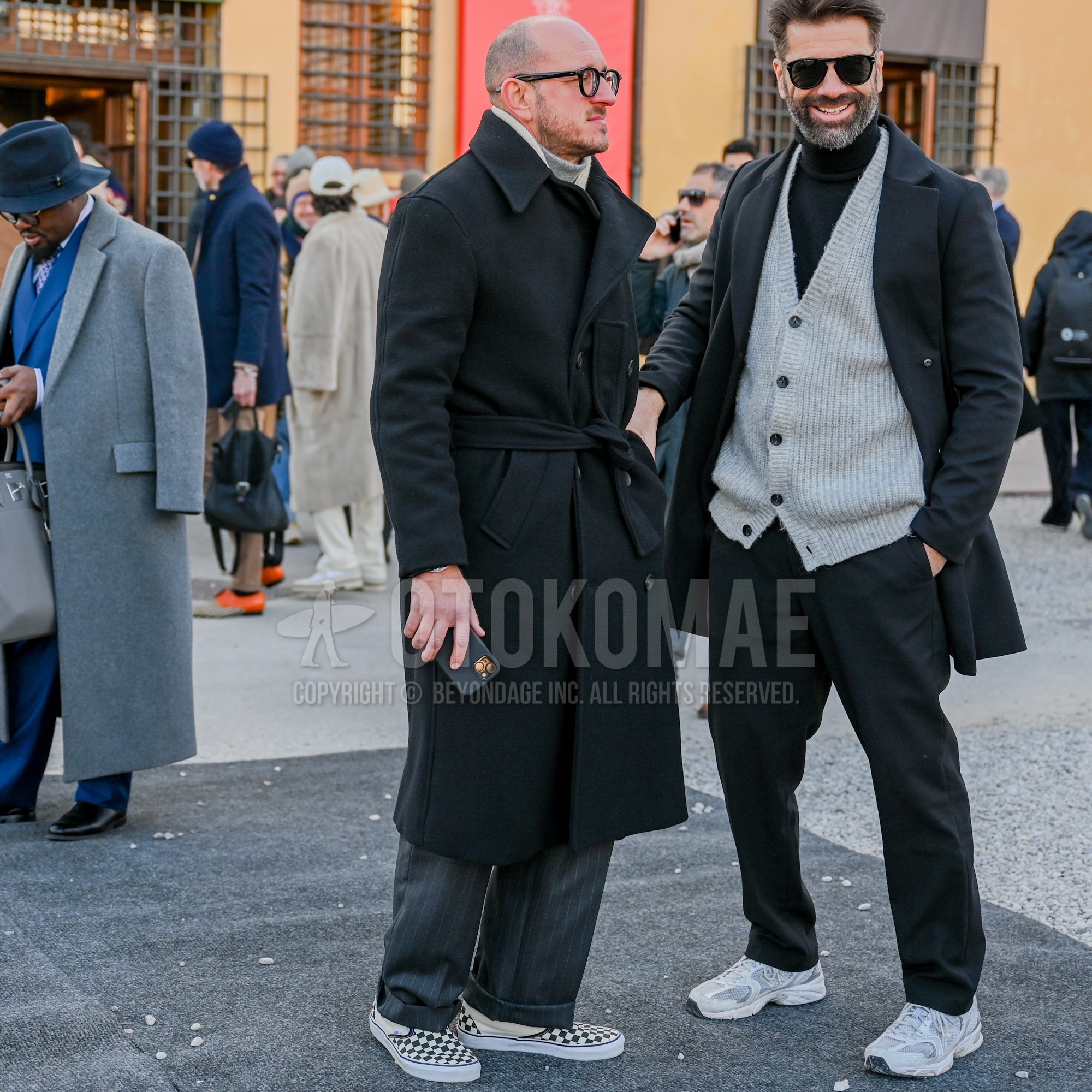 黒無地のメガネ、黒無地のトレンチコート、グレーストライプのスラックス、バンズの白・黒スリッポンのスニーカーを合わせた秋冬のメンズコーデ・着こなし。 | OTOKOMAE / 男前研究所